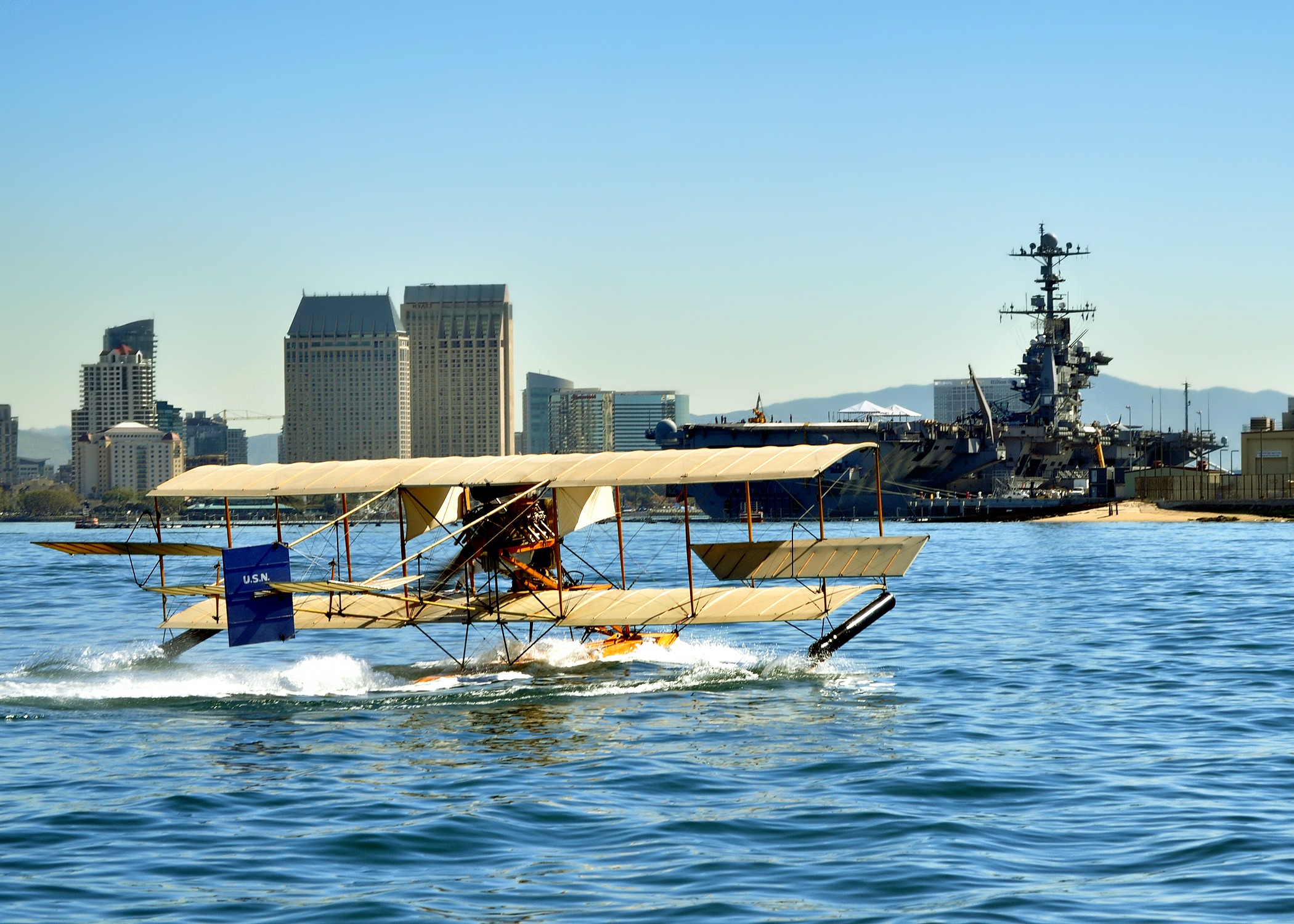 Seaplane taking off water in view of naval ship at city, usa ...