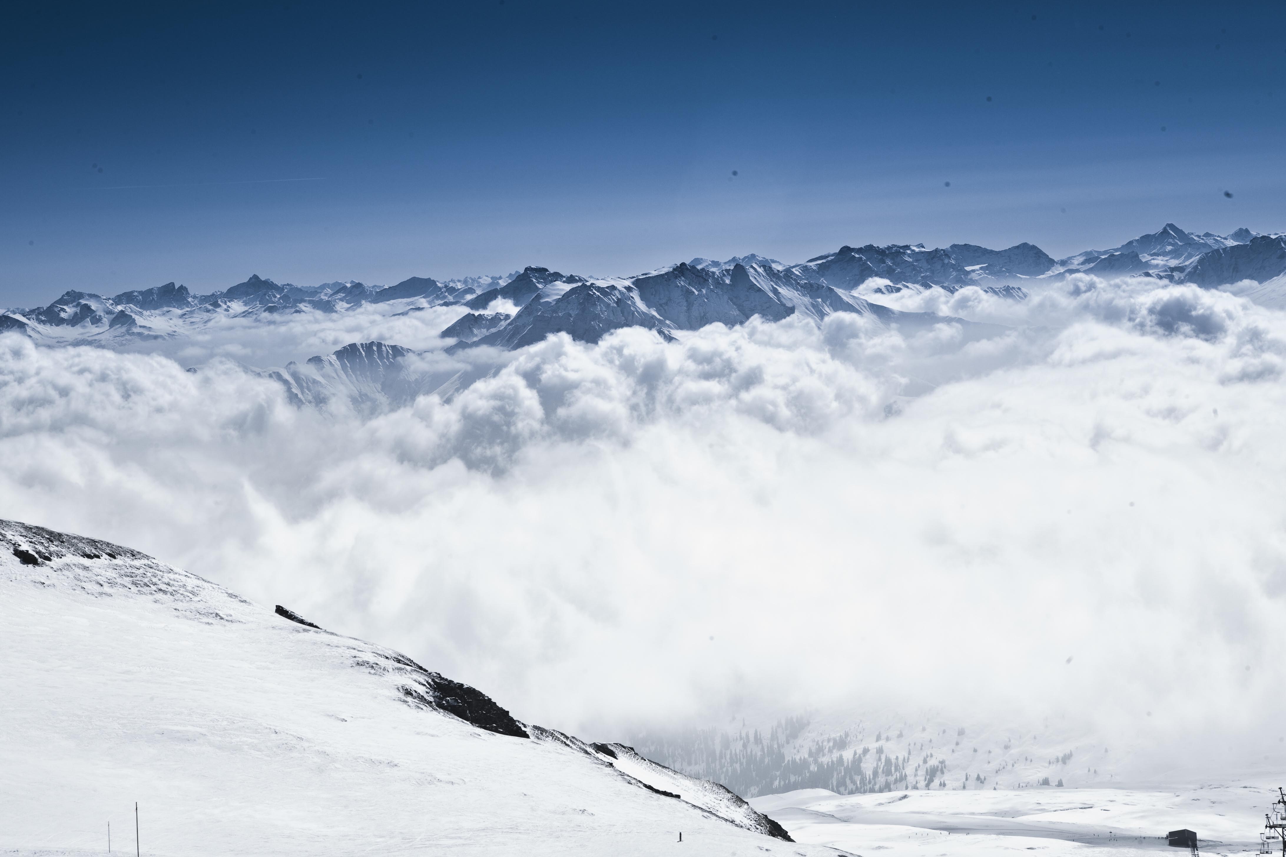 Ski path on snowy alpine mountains above clouds free image download